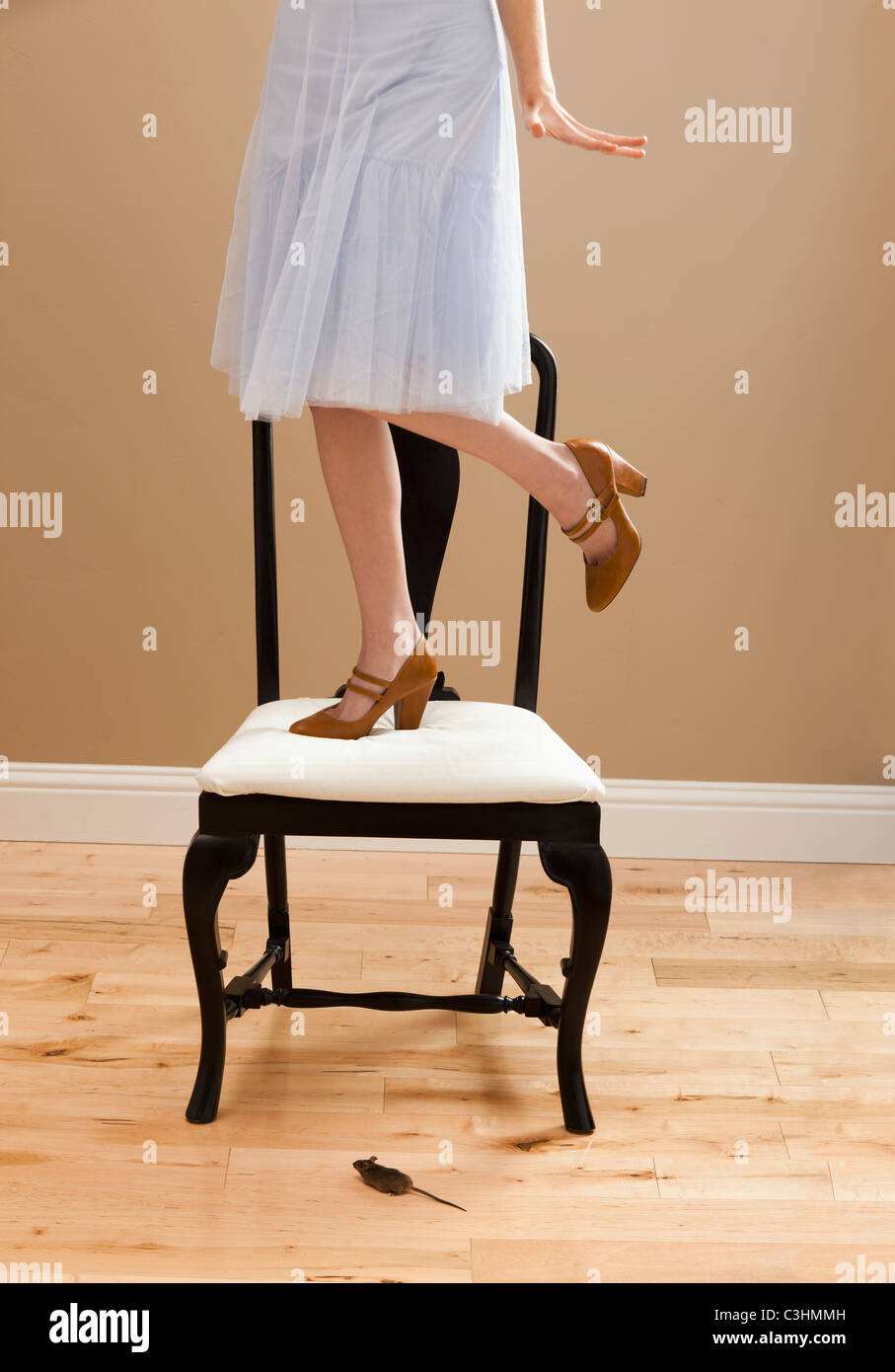 Young woman standing on chair, evading mouse Stock Photo - Alamy