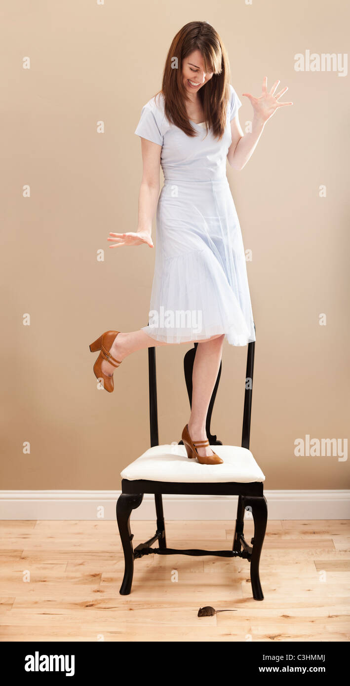 Young woman standing on chair, evading mouse Stock Photo - Alamy