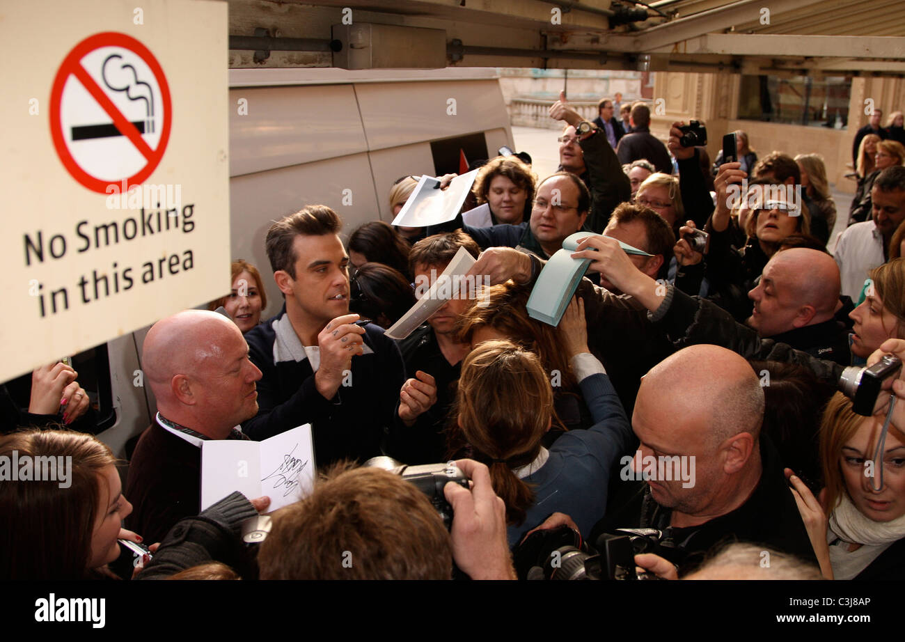 Robbie Williams signs autographs for fans while smoking a cigarette ...