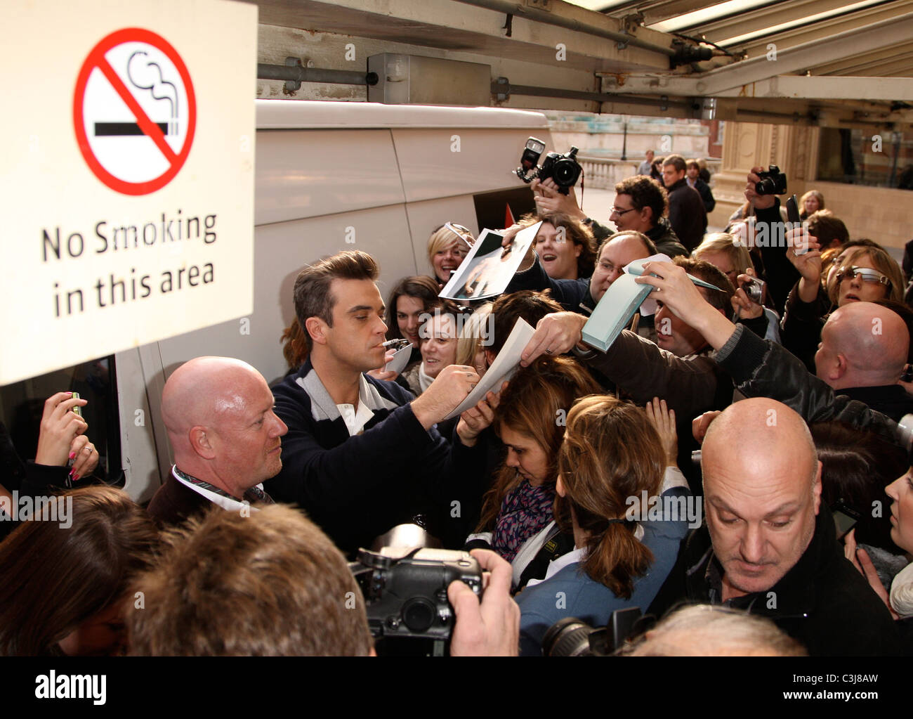 Robbie Williams signs autographs for fans while smoking a cigarette ...
