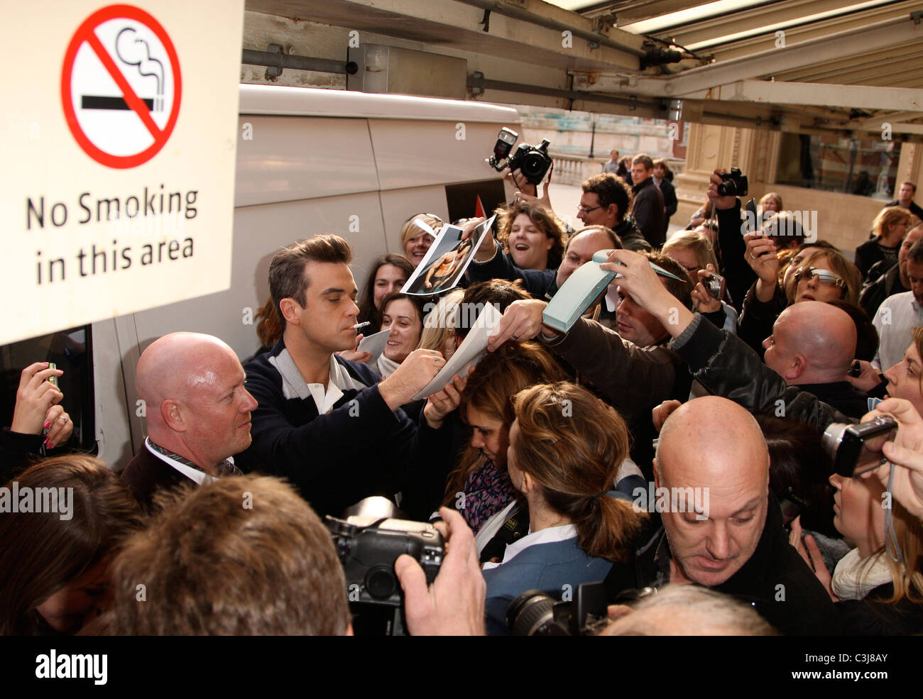 Robbie Williams signs autographs for fans while smoking a cigarette ...