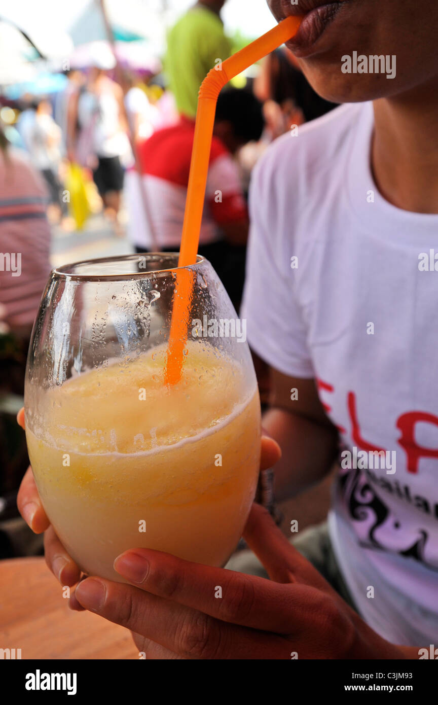 thai girl drinking iced peach juicy drink in a large pitcher glass ...