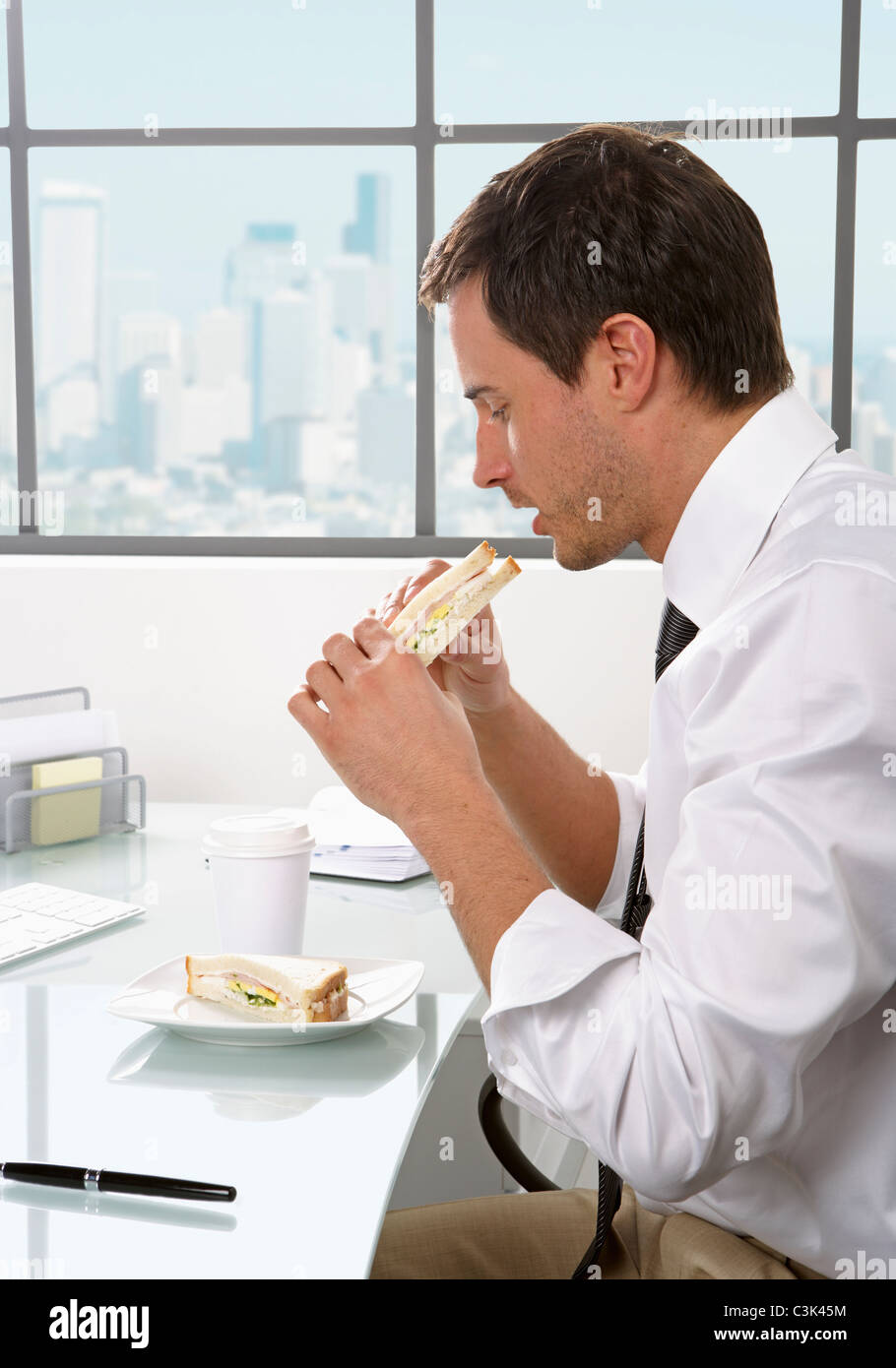 Businessman eating sandwich at his desk Stock Photo - Alamy