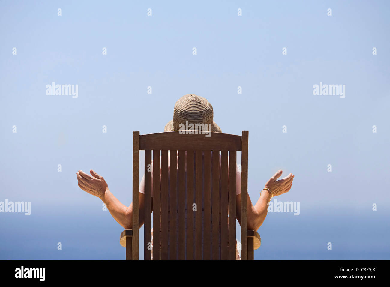Rear view of woman sitting on wooden chair, facing sea Stock Photo - Alamy