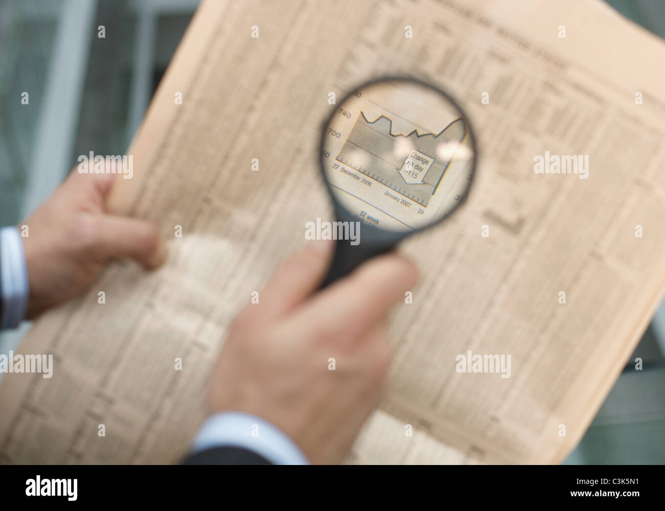 Man holding a magnifying glass over a newspaper Stock Photo - Alamy
