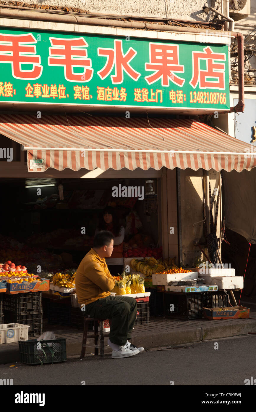 Man sitting in a shop front looks towards the setting sun in Shanghai ...