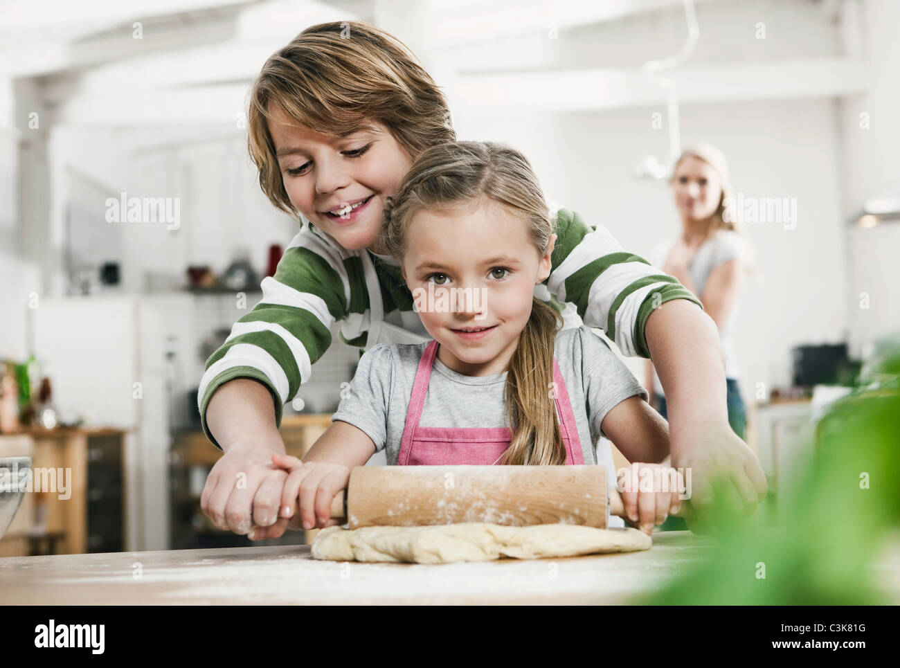 Germany, Cologne, Boy and girl rolling dough, mother in background ...