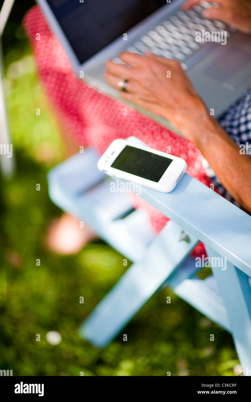 Women using laptop, focus on mobile phone on chair Stock Photo - Alamy