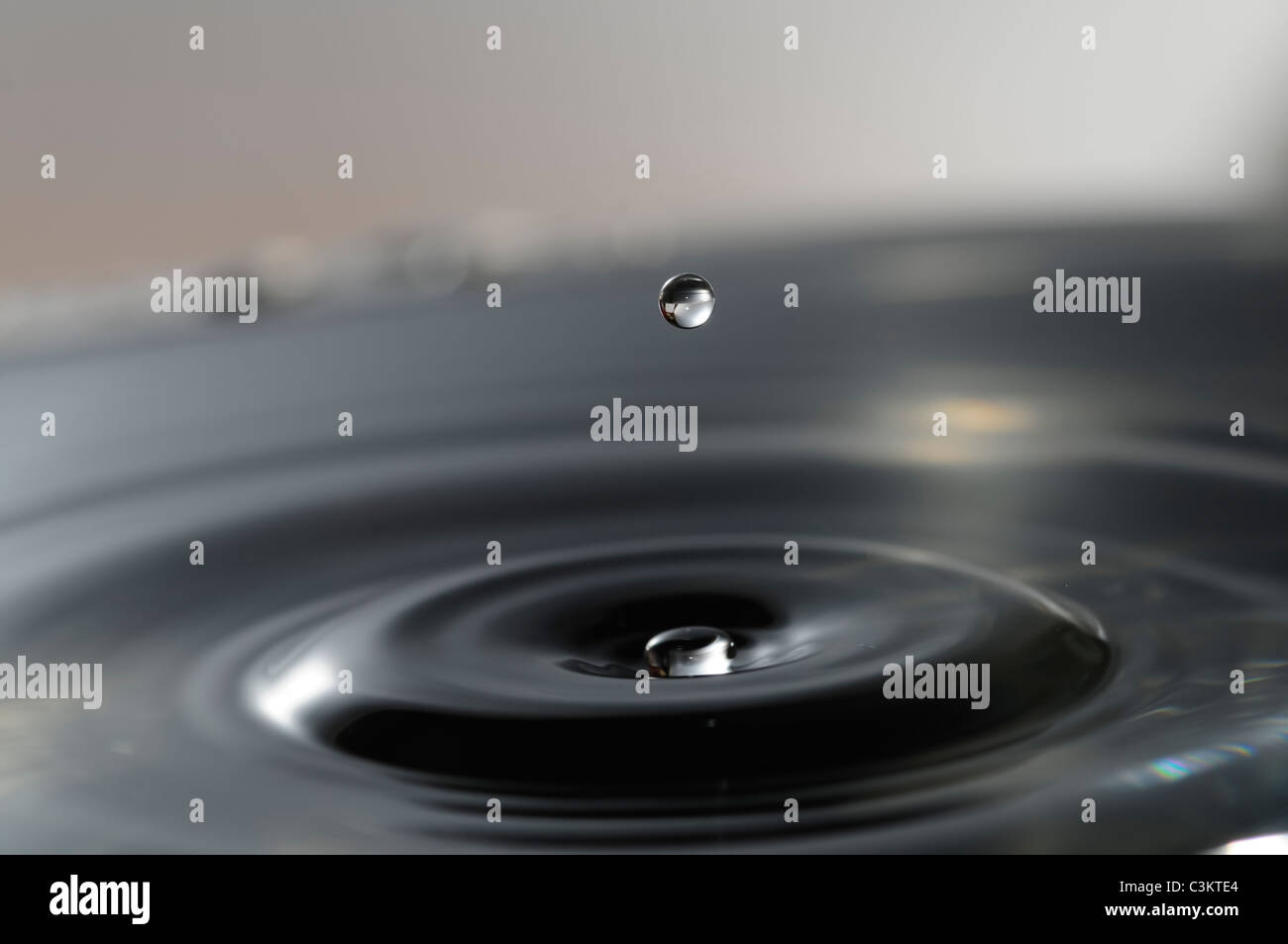 Droplet of water floating above a ripple in a bowl of silvery water ...