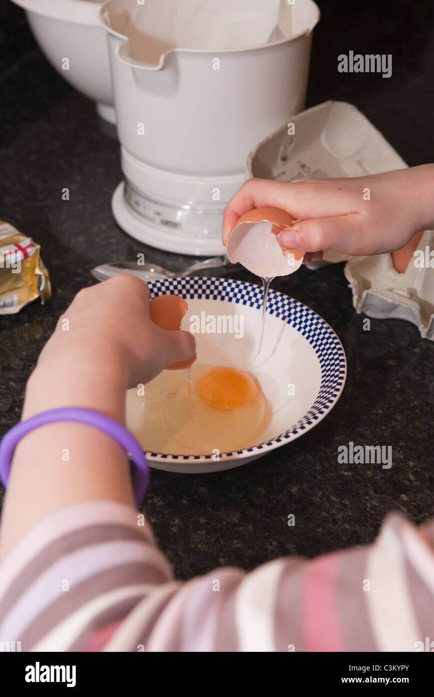 Young girl cracking an egg (holding shell in hands as white pours into ...