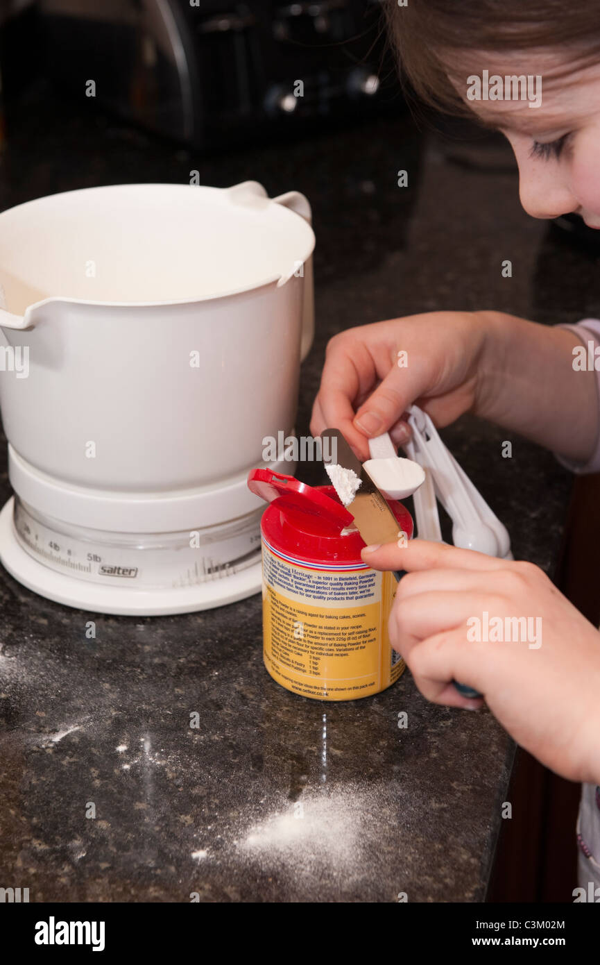 Young girl cooking, measuring baking powder using knife to get level ...
