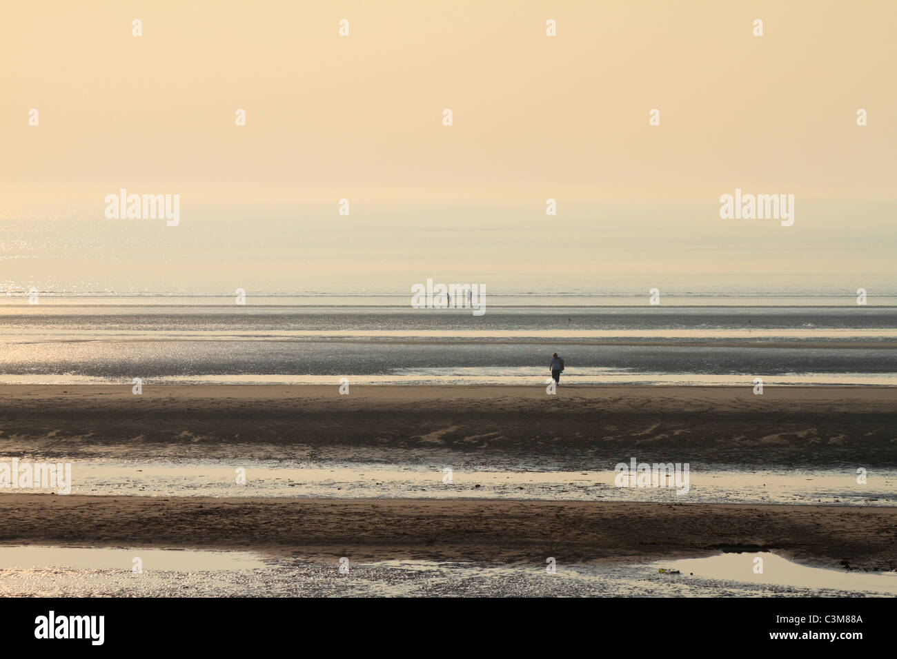 Three lone people walking on Formby beach in late afternoon sunshine ...