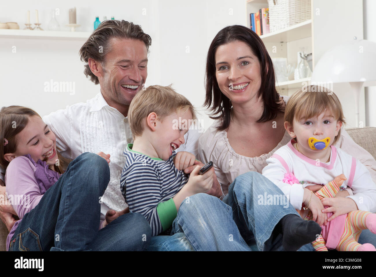 Germany, Bavaria, Munich, Family sitting together on couch, laughing ...
