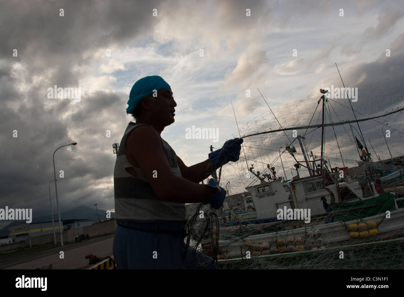A fisherman works on his boat in the port of Shikabe, Hokkaido, Japan ...