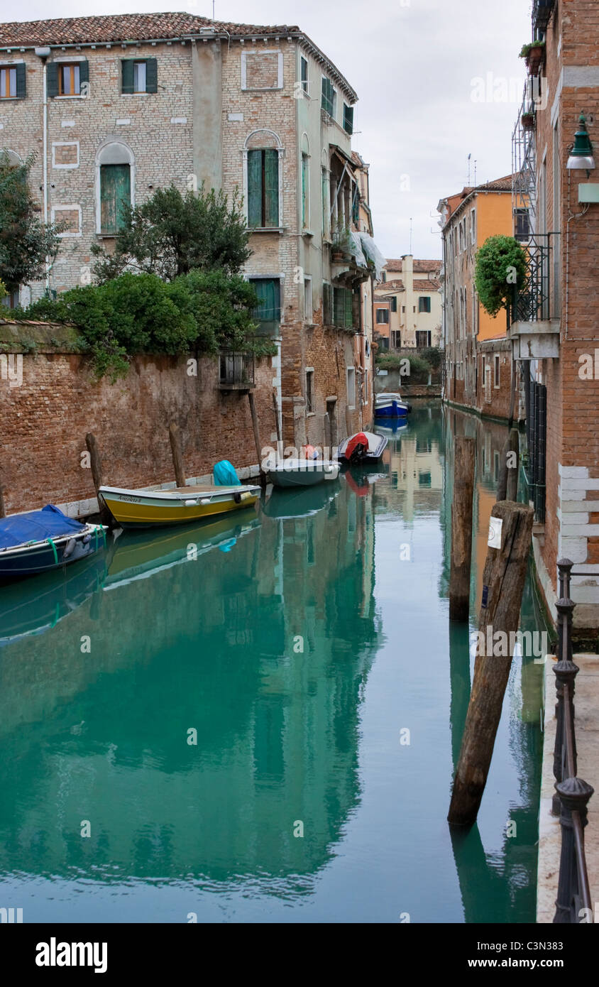 A quiet backwater in Venice, Italy with houses and boats reflected in ...