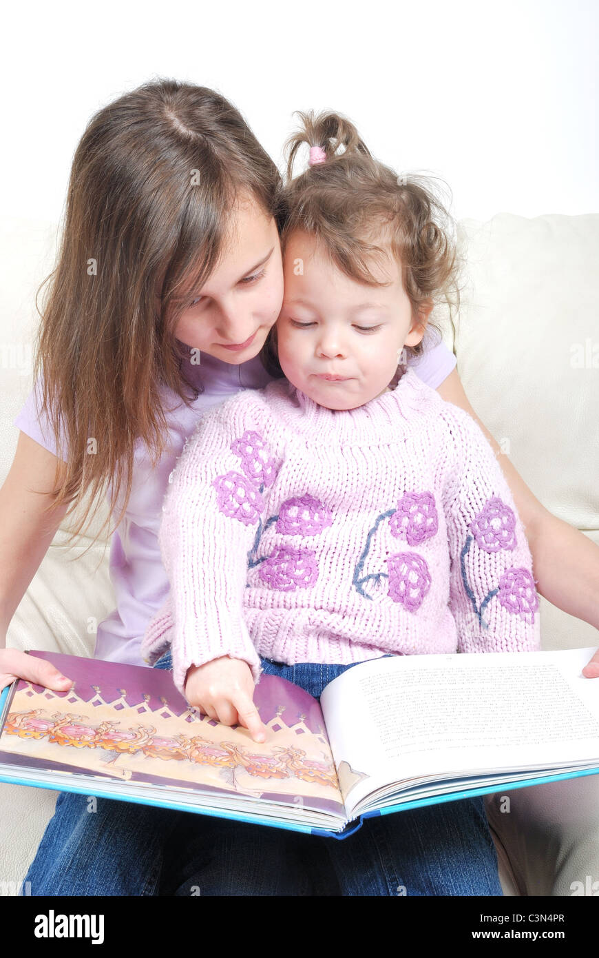 Sisters sitting in living room reading book Stock Photo - Alamy