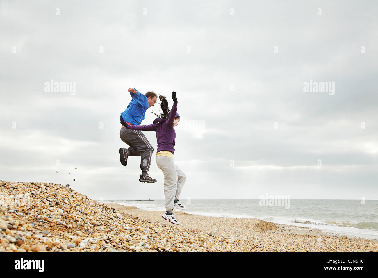 Couple jumping on beach on cloudy day Stock Photo - Alamy