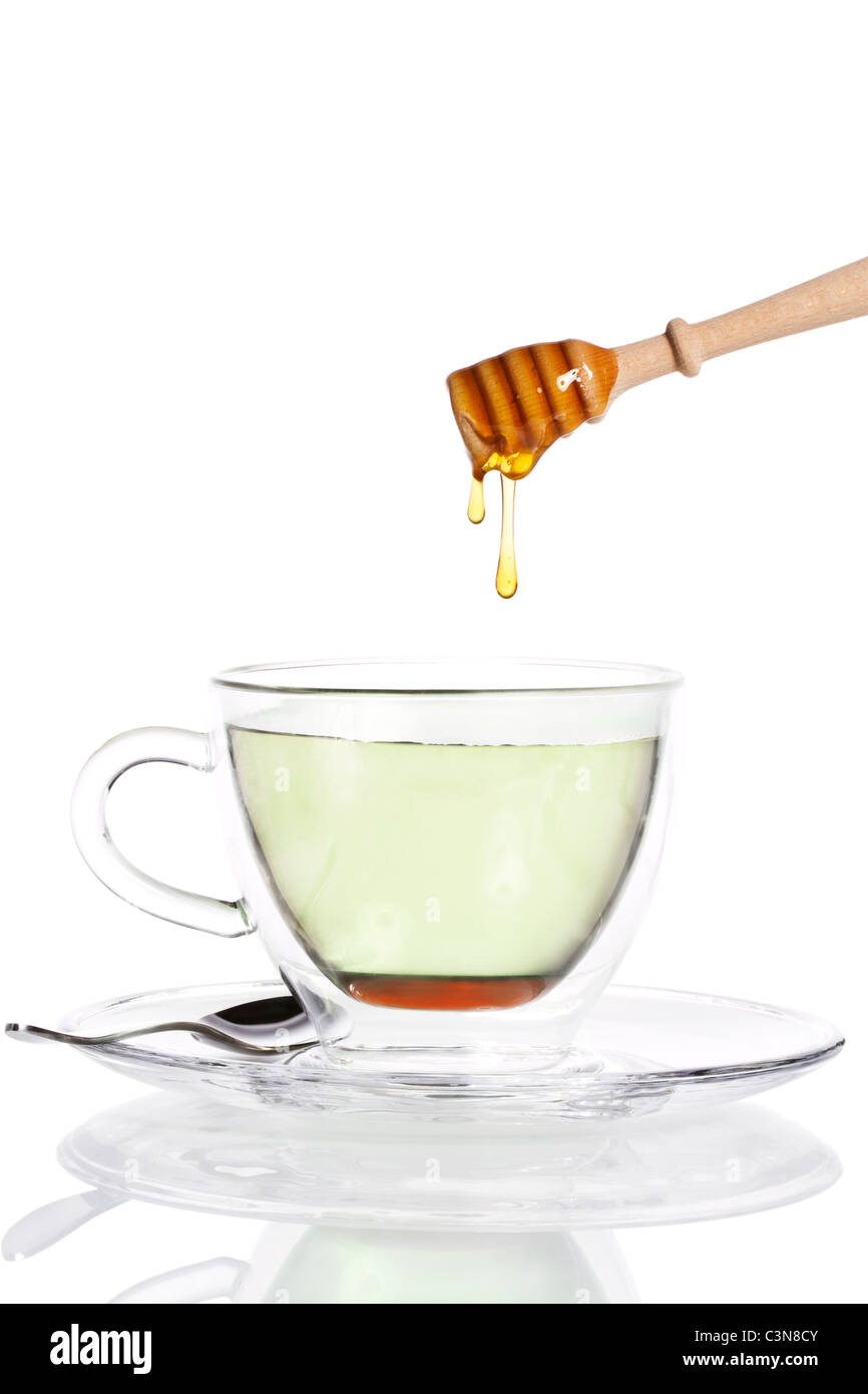 honey drops from a honey dipper in glass cup with green tea on white ...