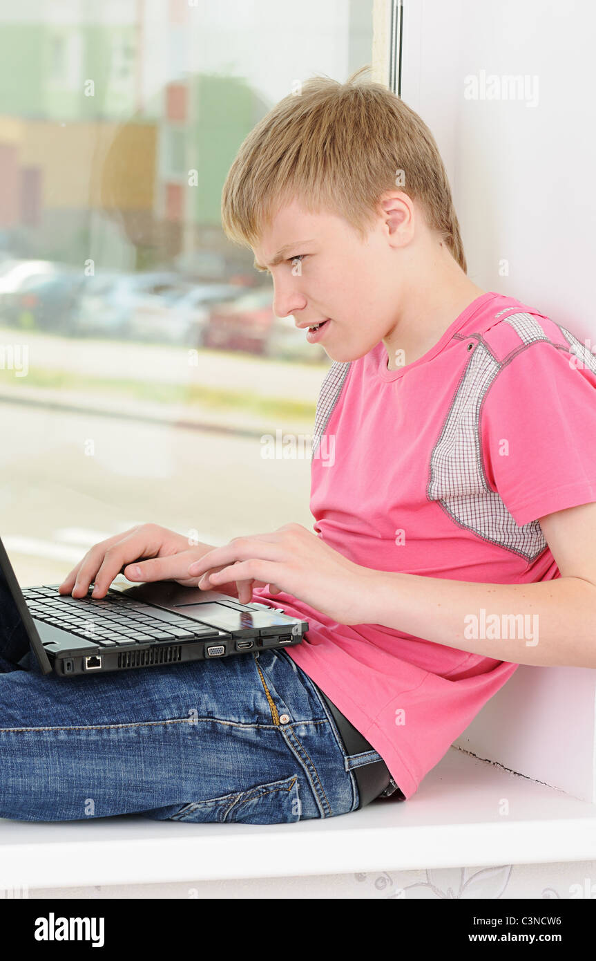 The joyful teenager with a computer sits on a window Stock Photo - Alamy