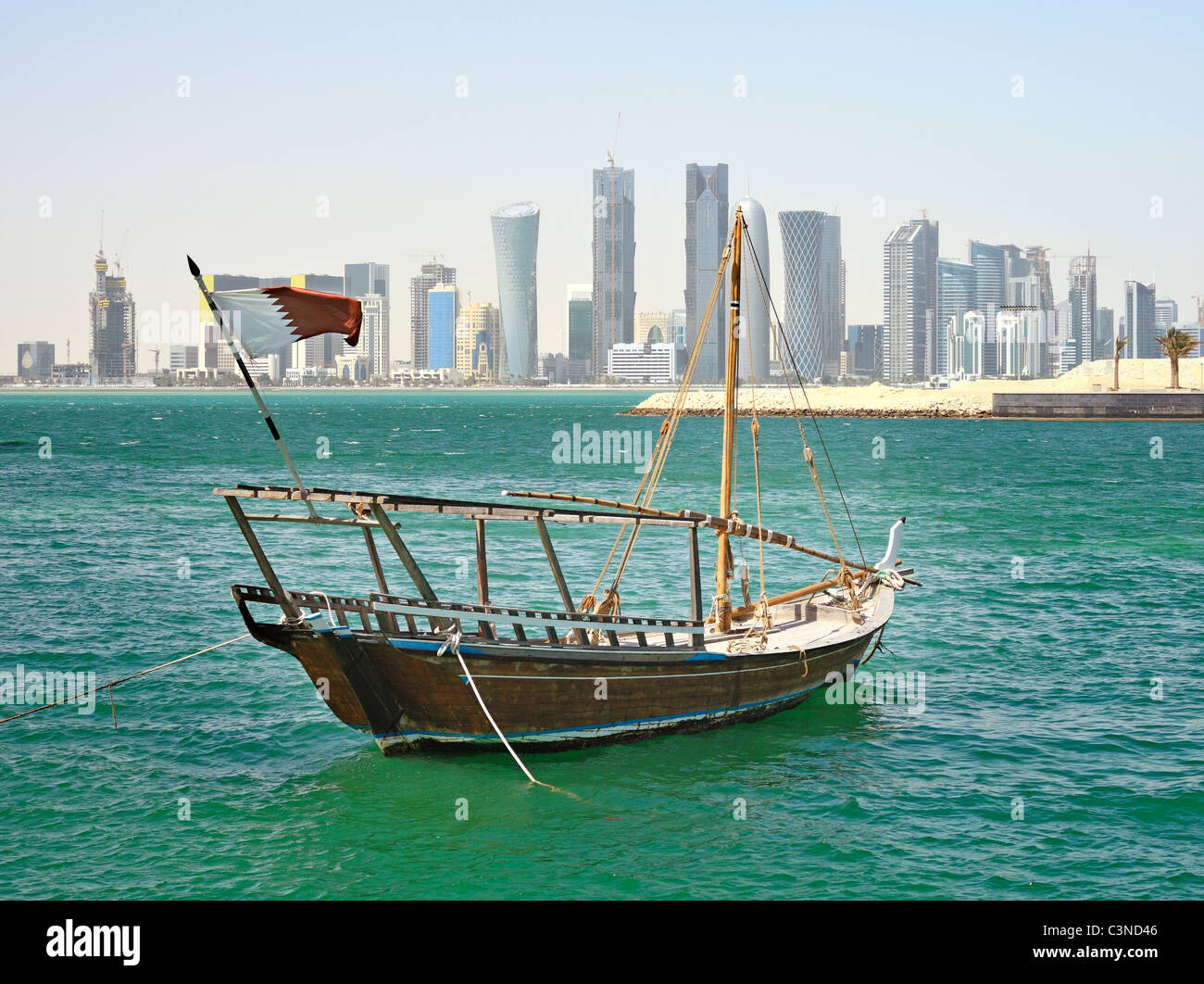 A small Qatari sailing dhow, with the national flag flying and the Doha ...