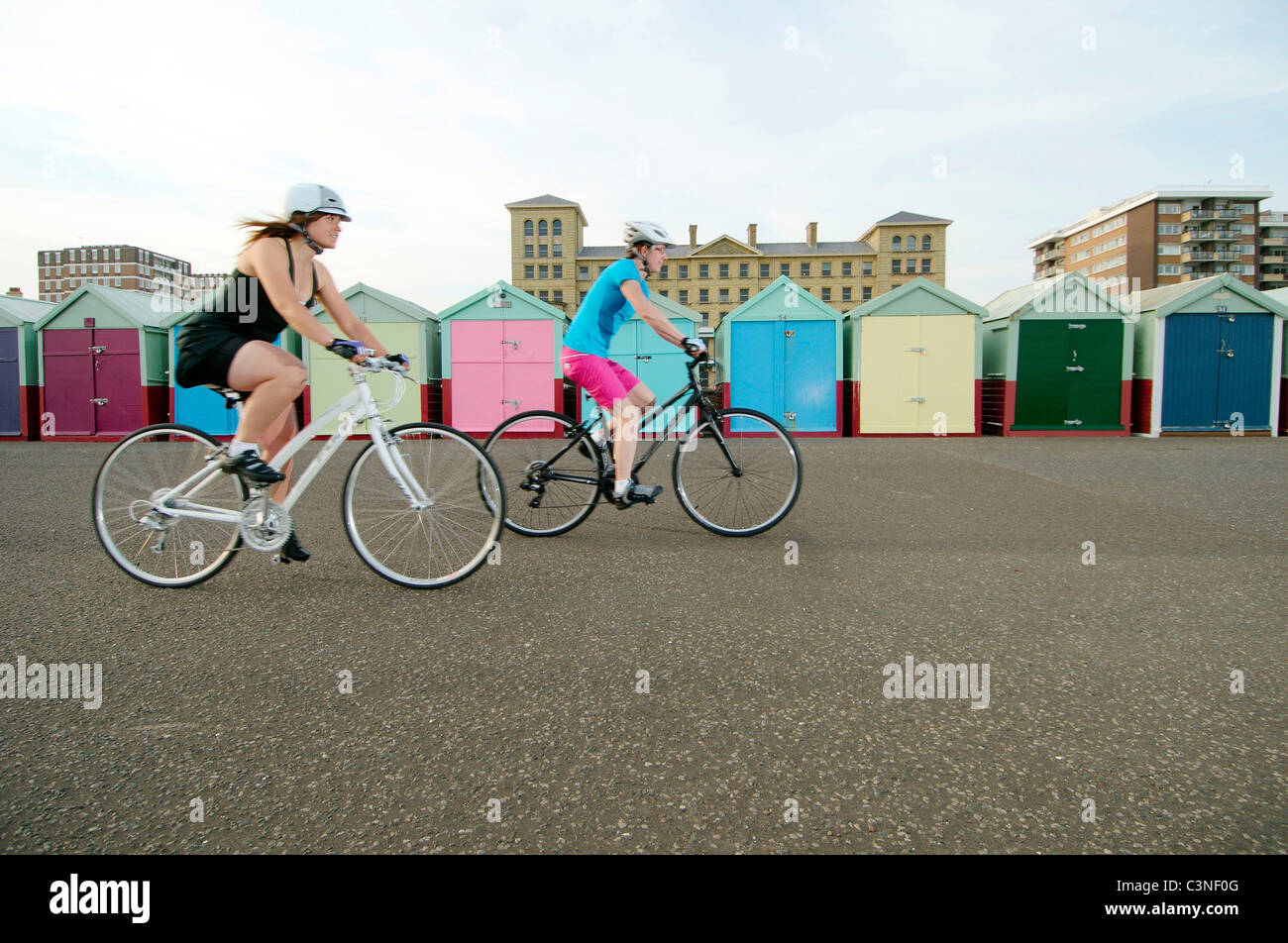 women riding their bicycles past coloured beach hits. Brighton seafront ...