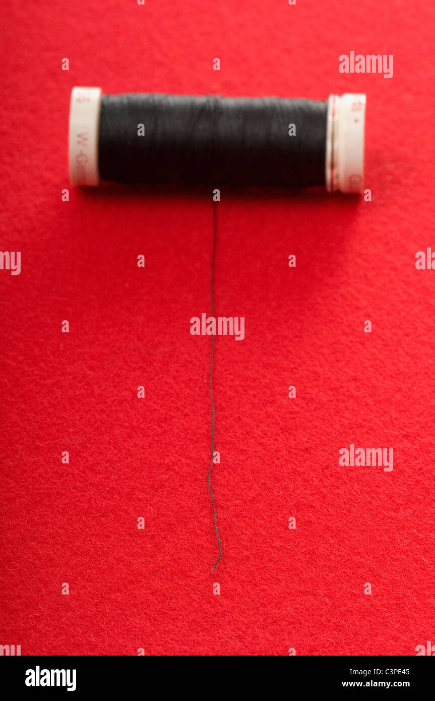Black thread reel on red background Stock Photo - Alamy