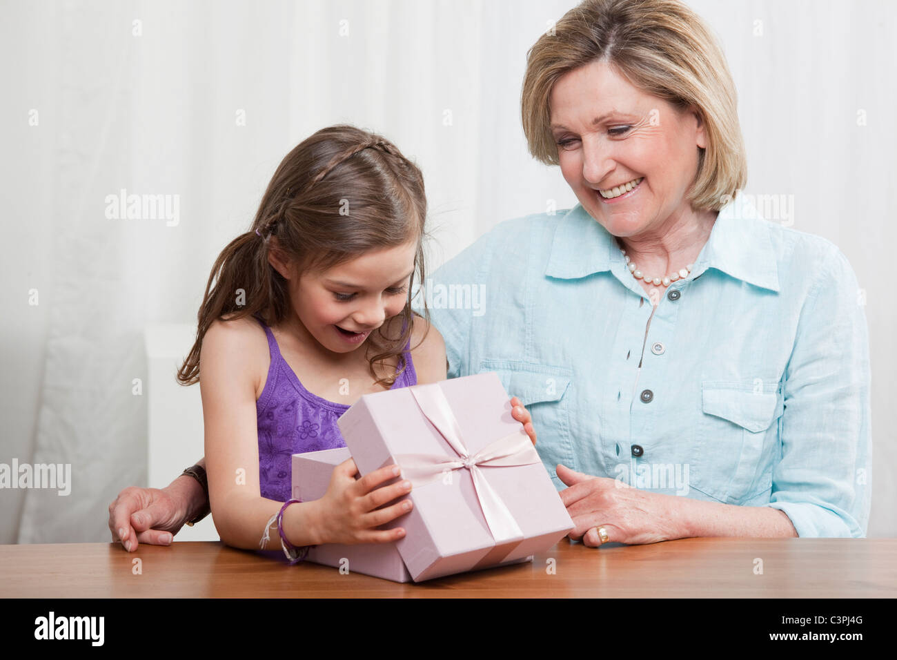 Granddaughter (6-7) opening gift box and grandmother smiling Stock ...
