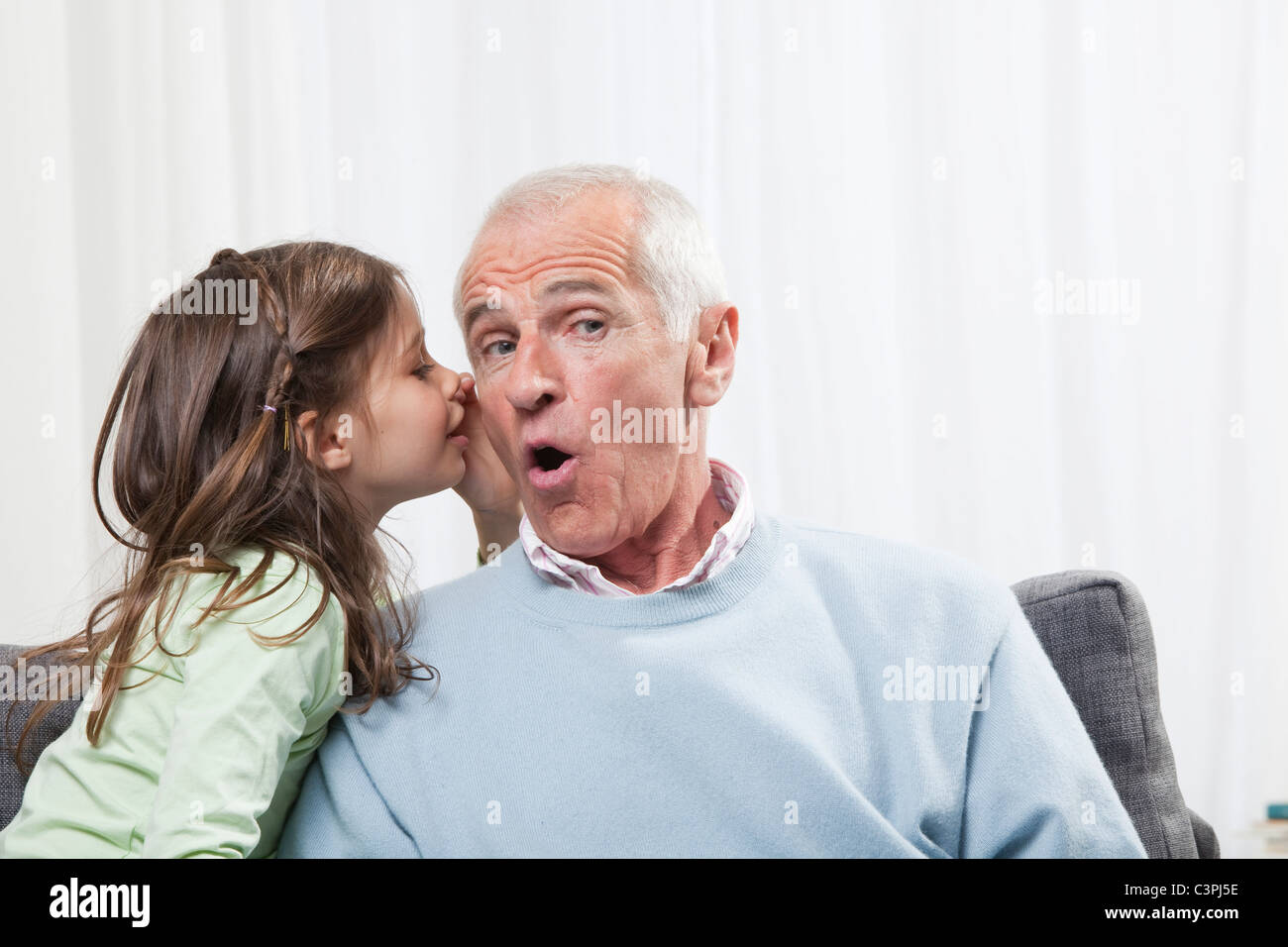 Girl (6-7) whispering into grandfather's ear, close-up Stock Photo - Alamy