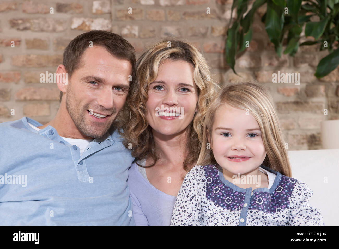 Germany, Cologne, Family sitting on sofa in living room, smiling ...