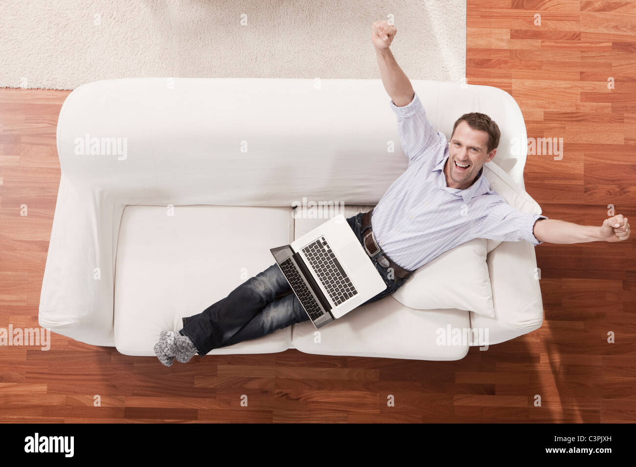 Germany, Cologne, Man with laptop on sofa, cheering, elevated view Stock Photo - Alamy