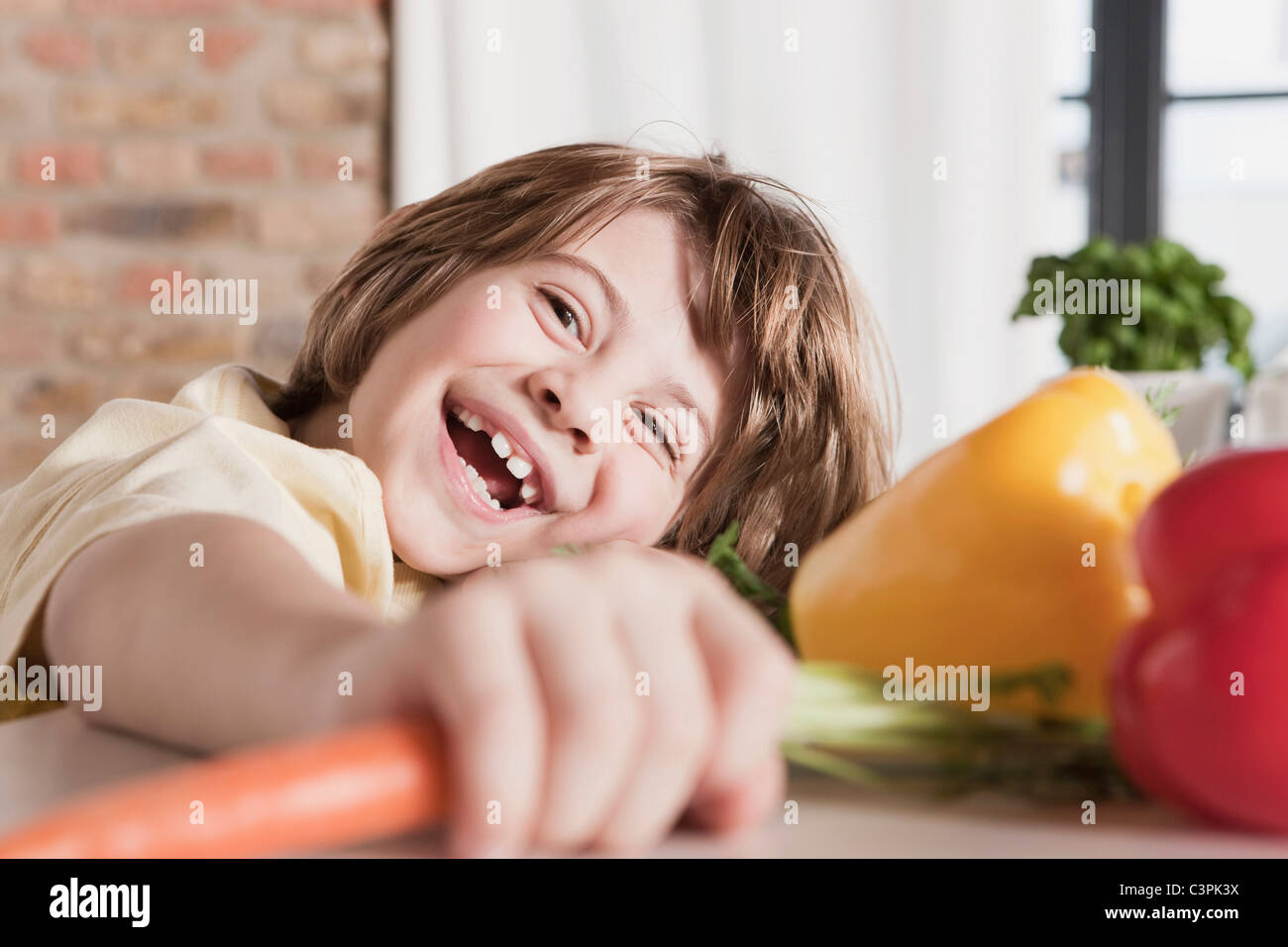 Germany, Cologne, Boy (6-7) in kitchen holding carrot, laughing ...
