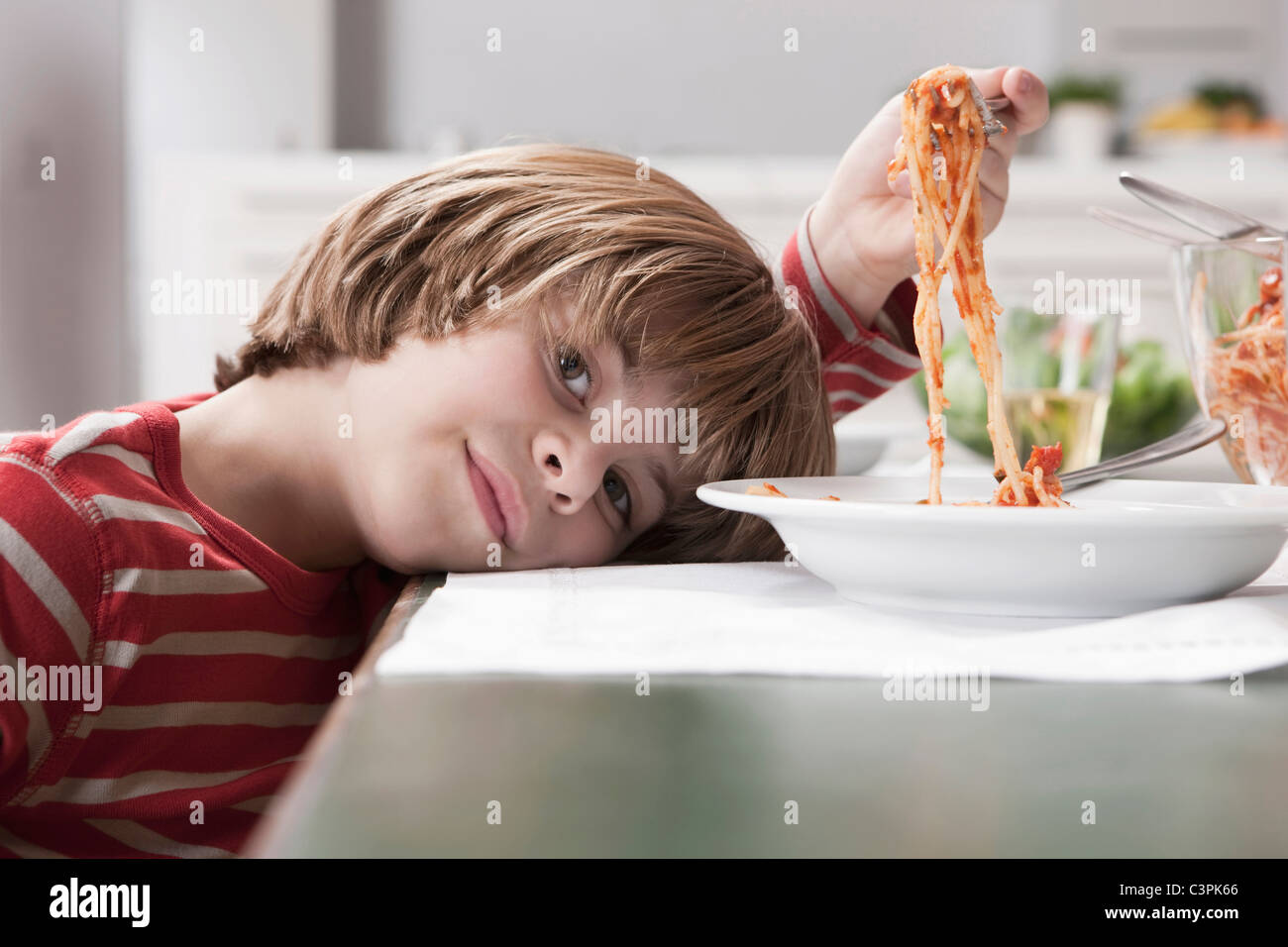 Germany, Cologne, Boy (6-7) sitting at table with head resting on table ...