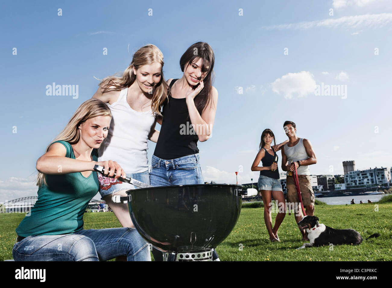Germany, Cologne, Women barbecueing and friends in background with dog ...