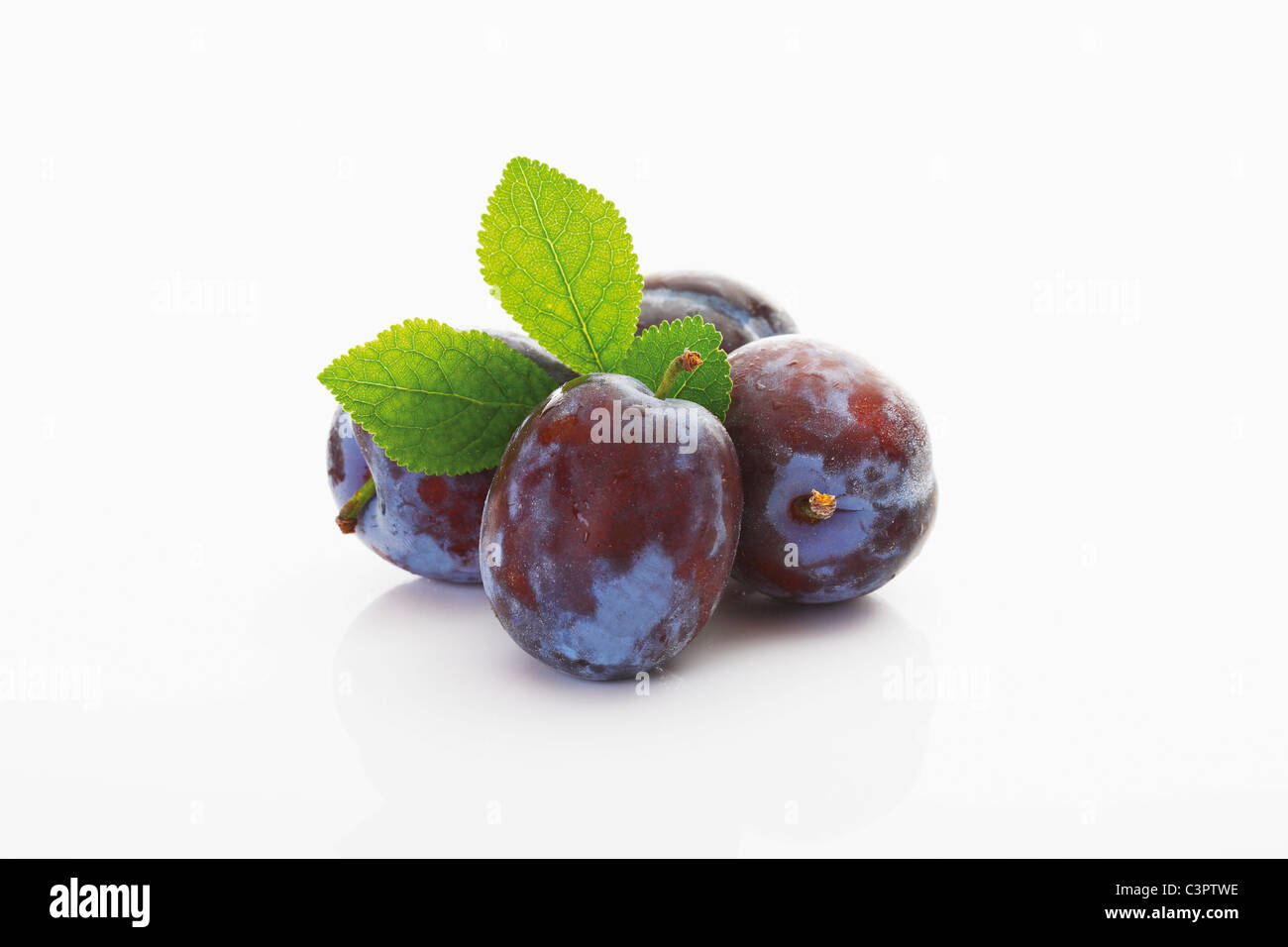 Four plums with leaves on white background, close up Stock Photo - Alamy
