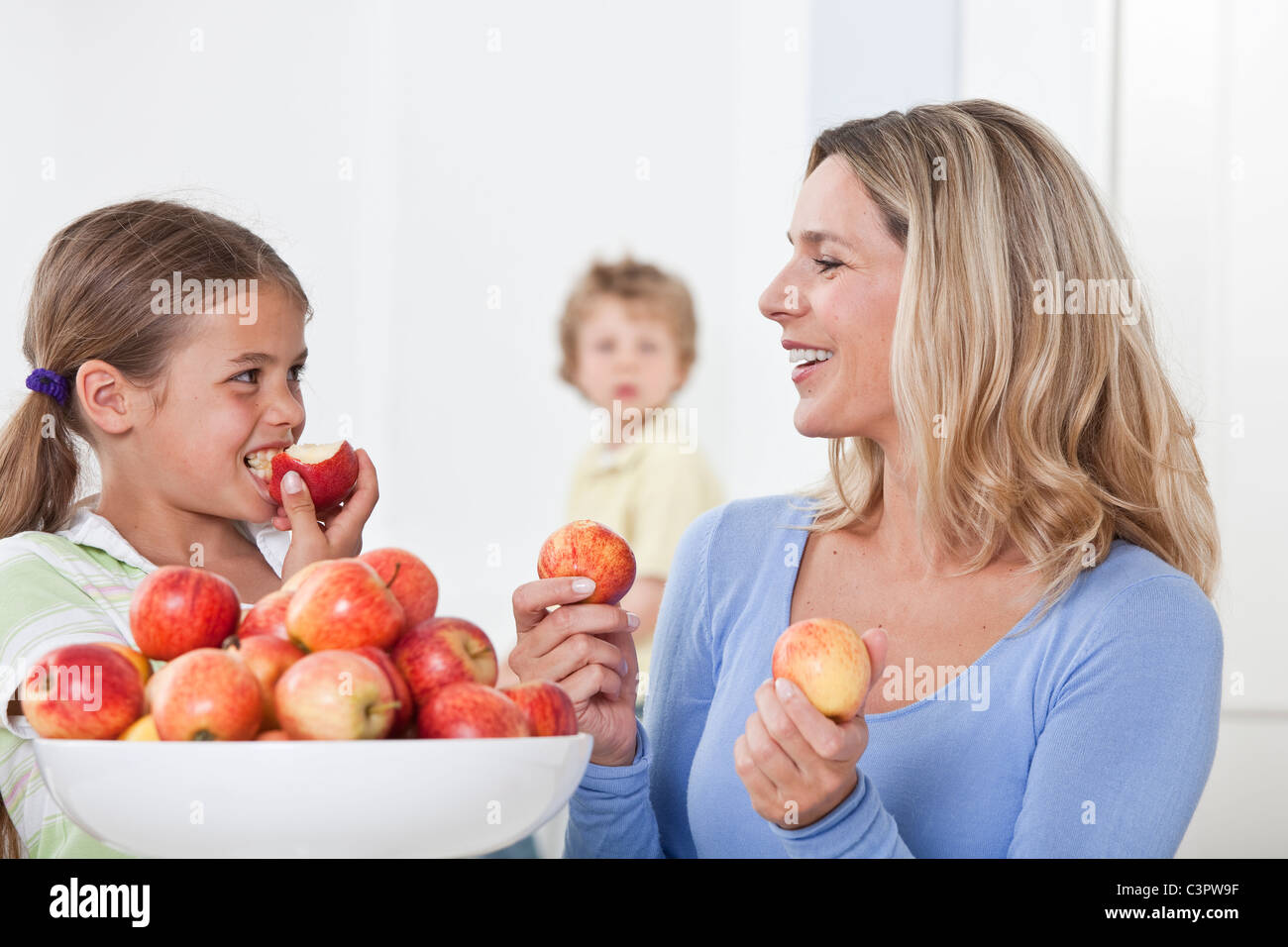 Mother and daughter eating apple with son in background Stock Photo - Alamy