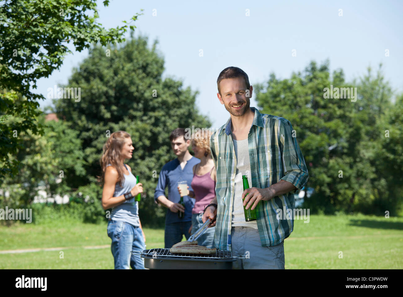 Germany, Munich, Man cooking food and friends in background Stock Photo ...