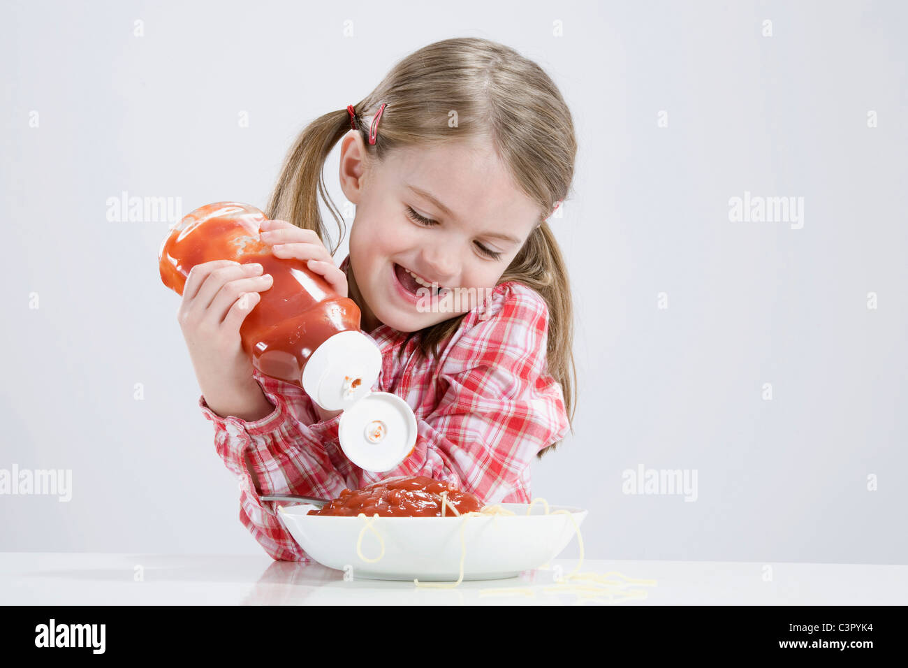 Girl (4-5) pouring ketchup on spagetti Stock Photo - Alamy