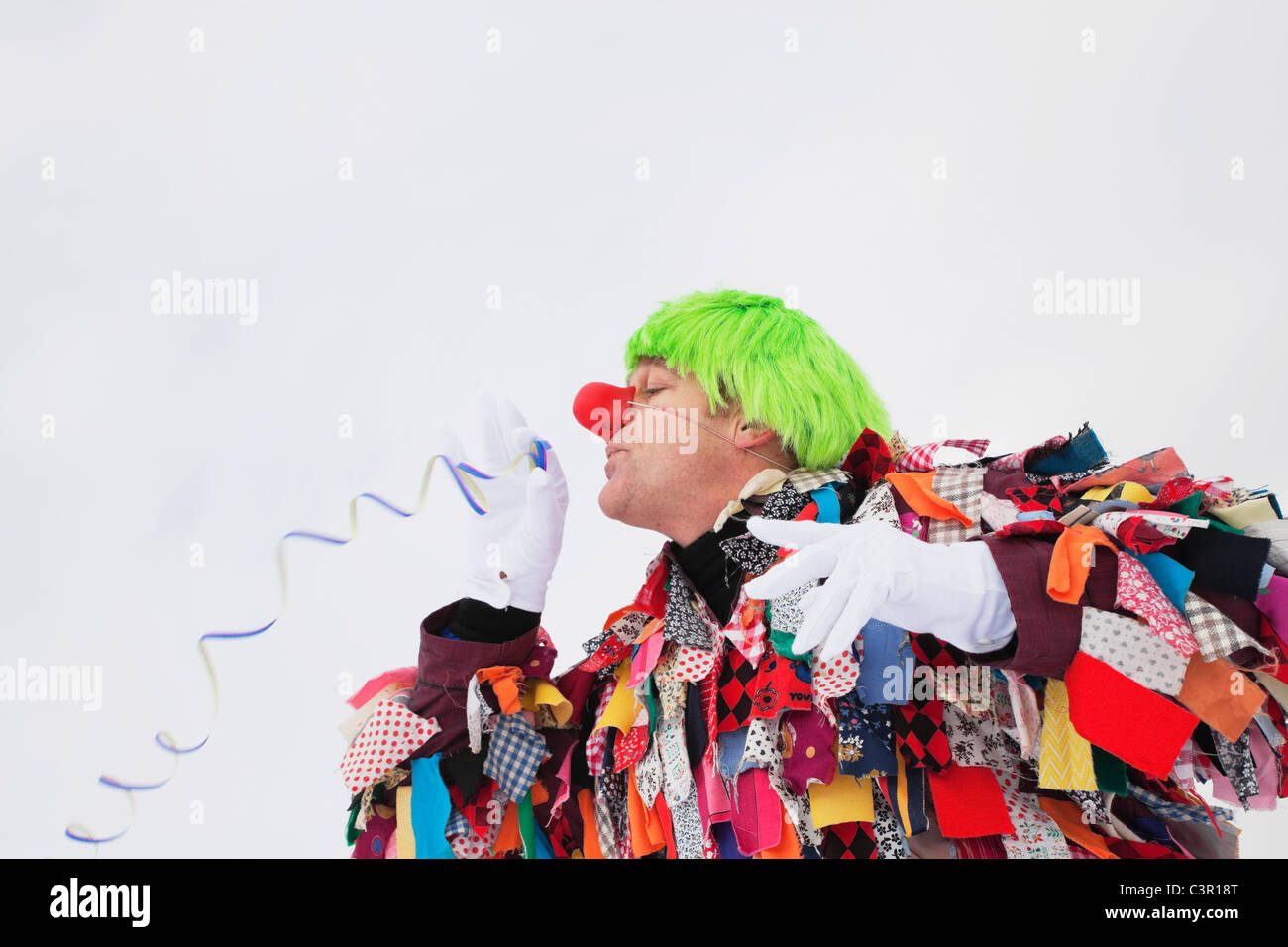 Germany, Cologne, Senior man in traditional costume blowing streamer ...