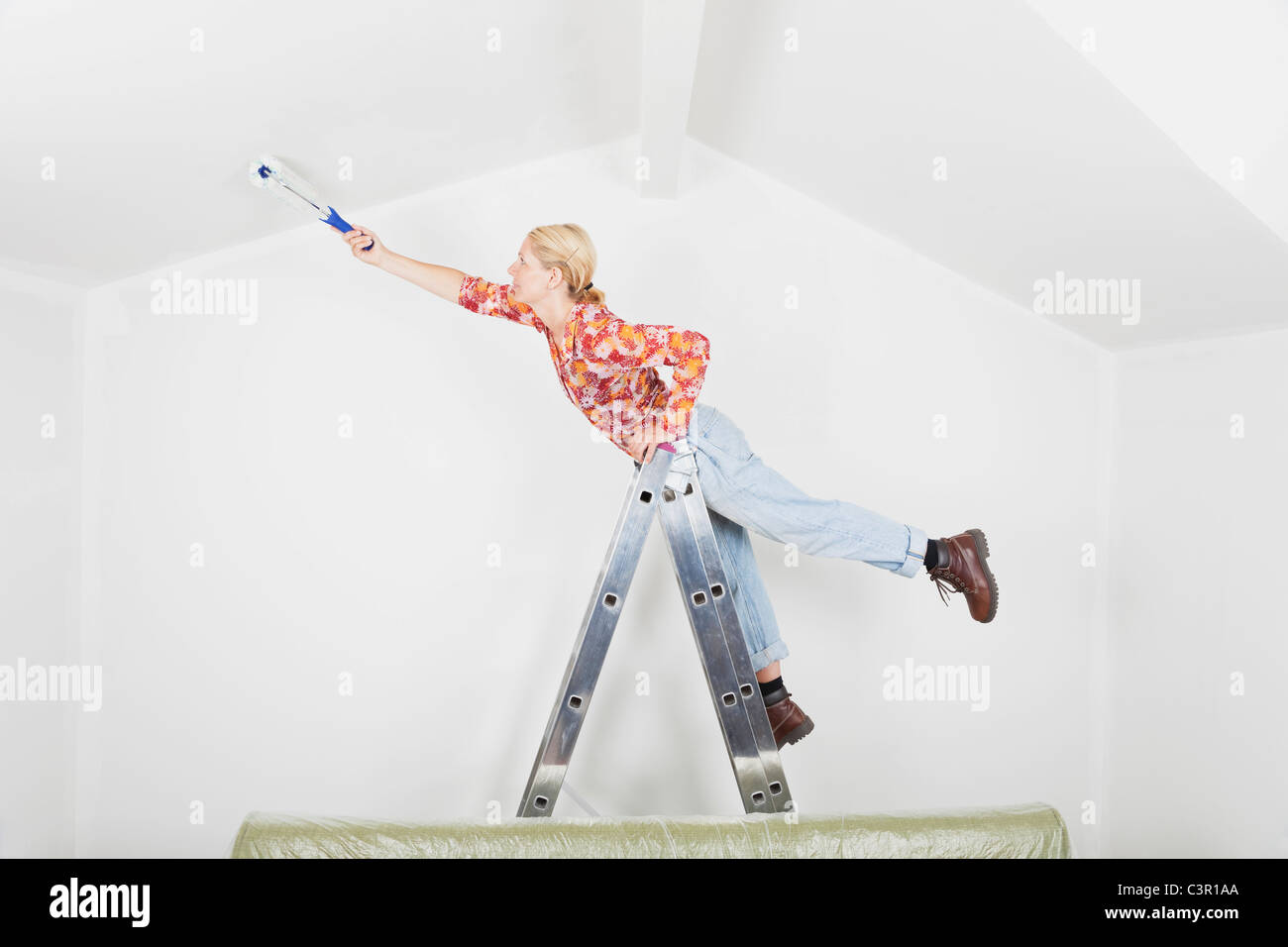 Germany, Cologne, Mature woman balancing on ladder during painting ...