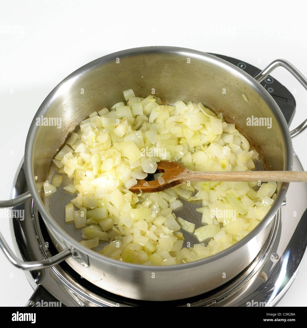 Frying onions in cooking pot with wooden spoon against white background ...