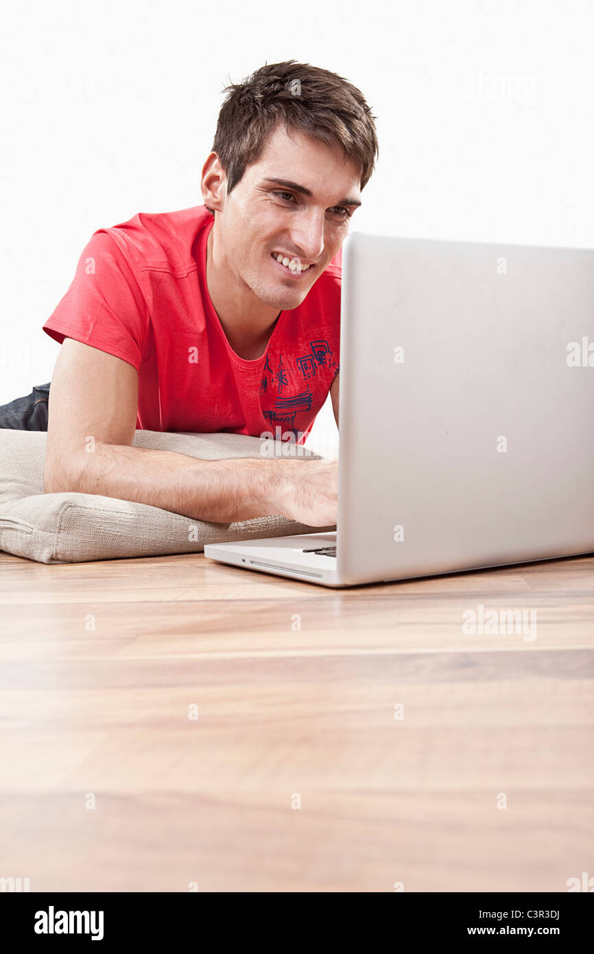 Young man lying on floor using laptop, smiling Stock Photo - Alamy