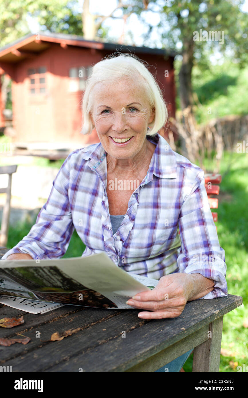 Germany, Saxony, Senior woman with newspaper at the farm, smiling ...