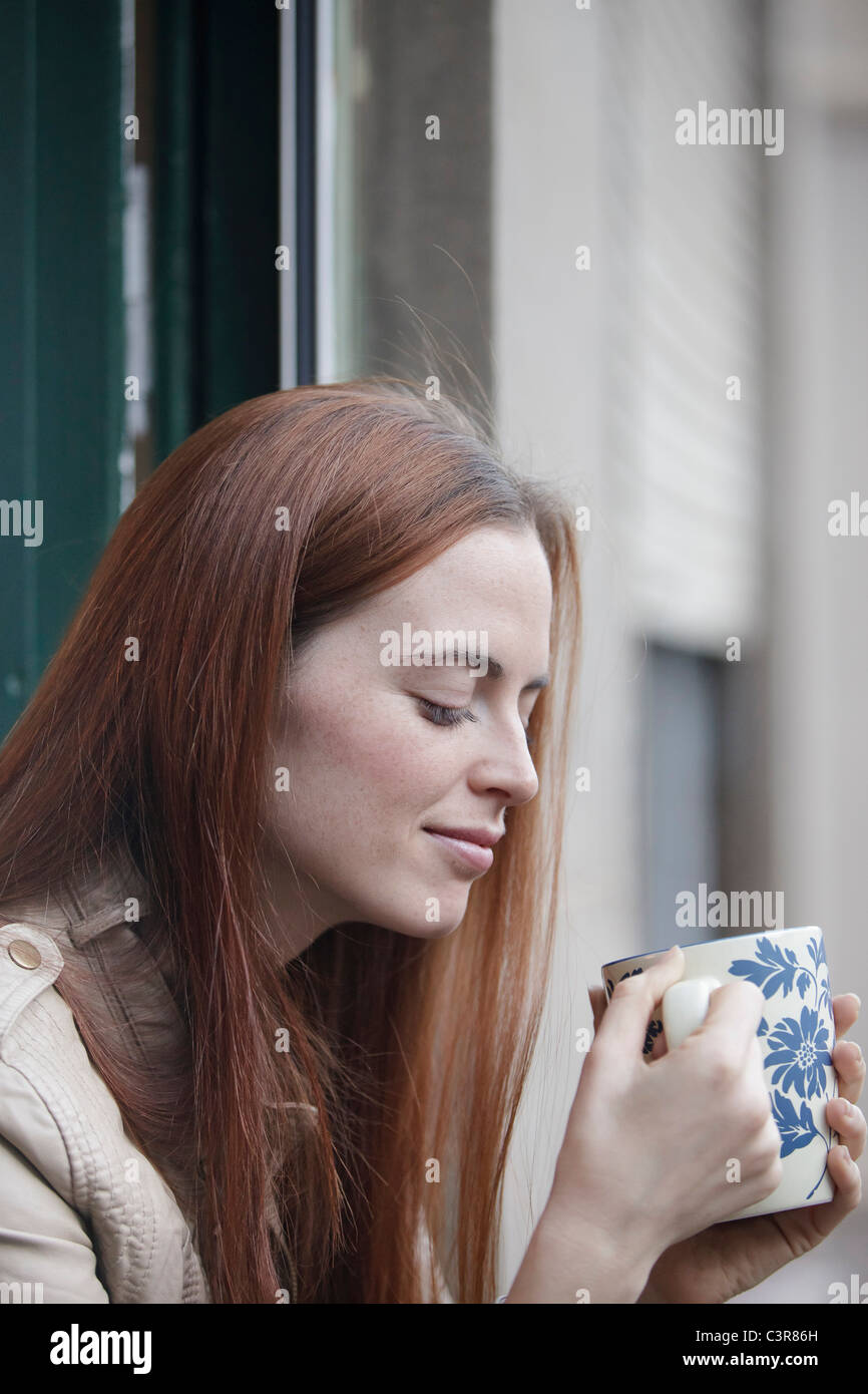 Woman leaning out of window holding cup Stock Photo - Alamy