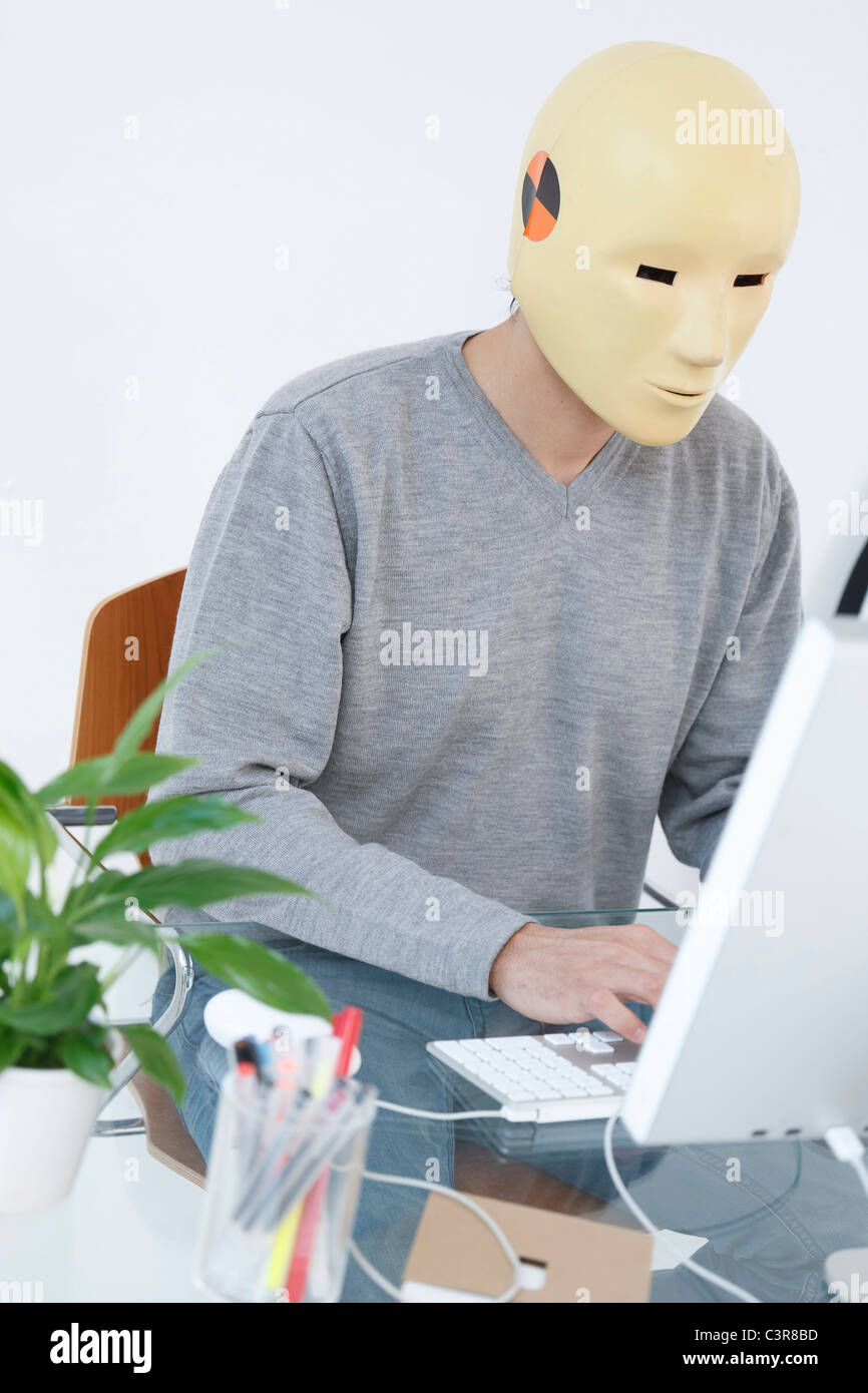 Man in crash dummy mask working at computer Stock Photo - Alamy