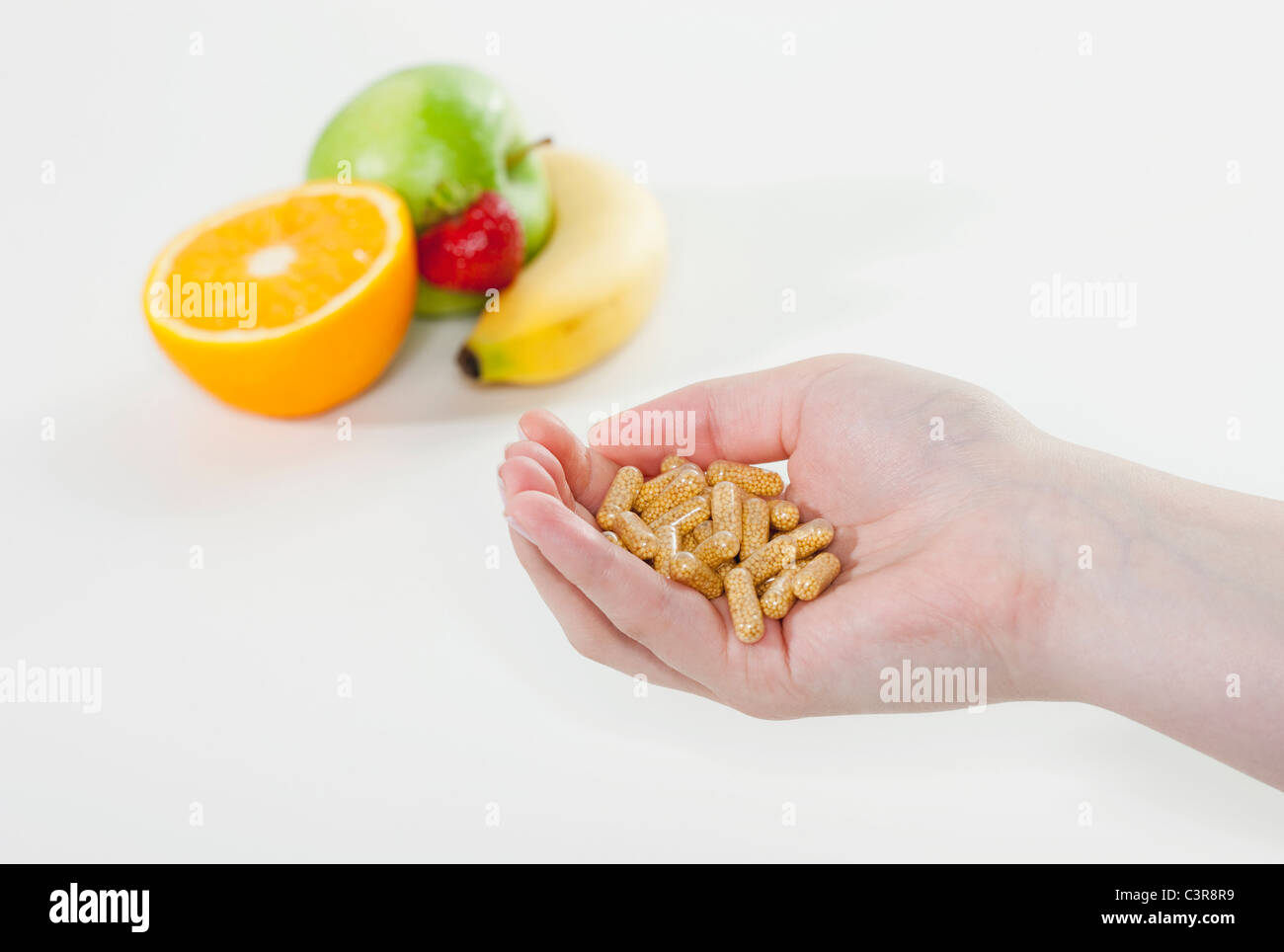 Germany, Cologne, Human hand holding pill with fruits in background ...