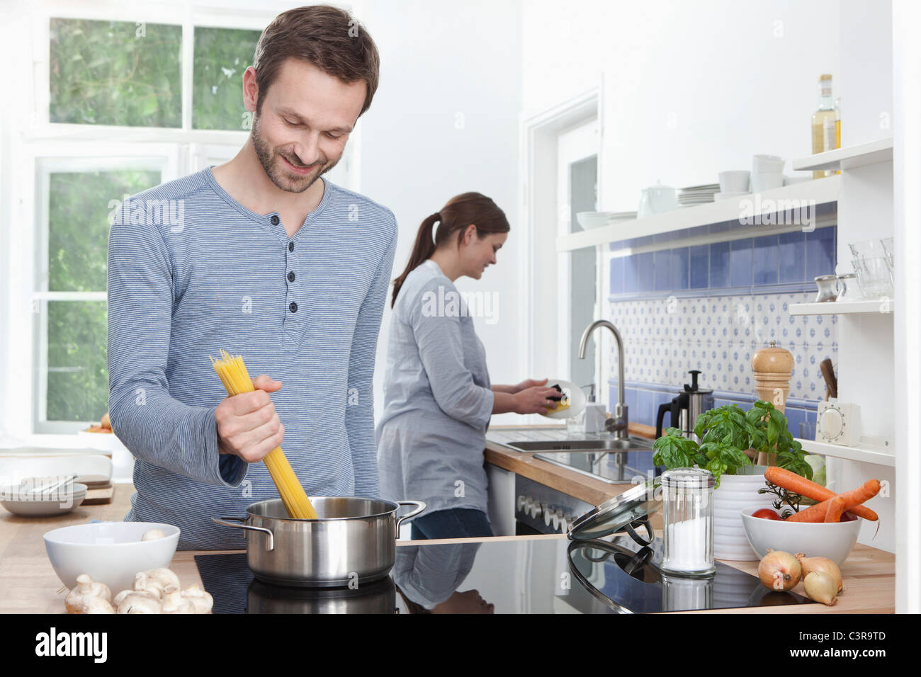 Germany, Bavaria, Munich, Man cooking spaghetti in kitchen, woman in ...
