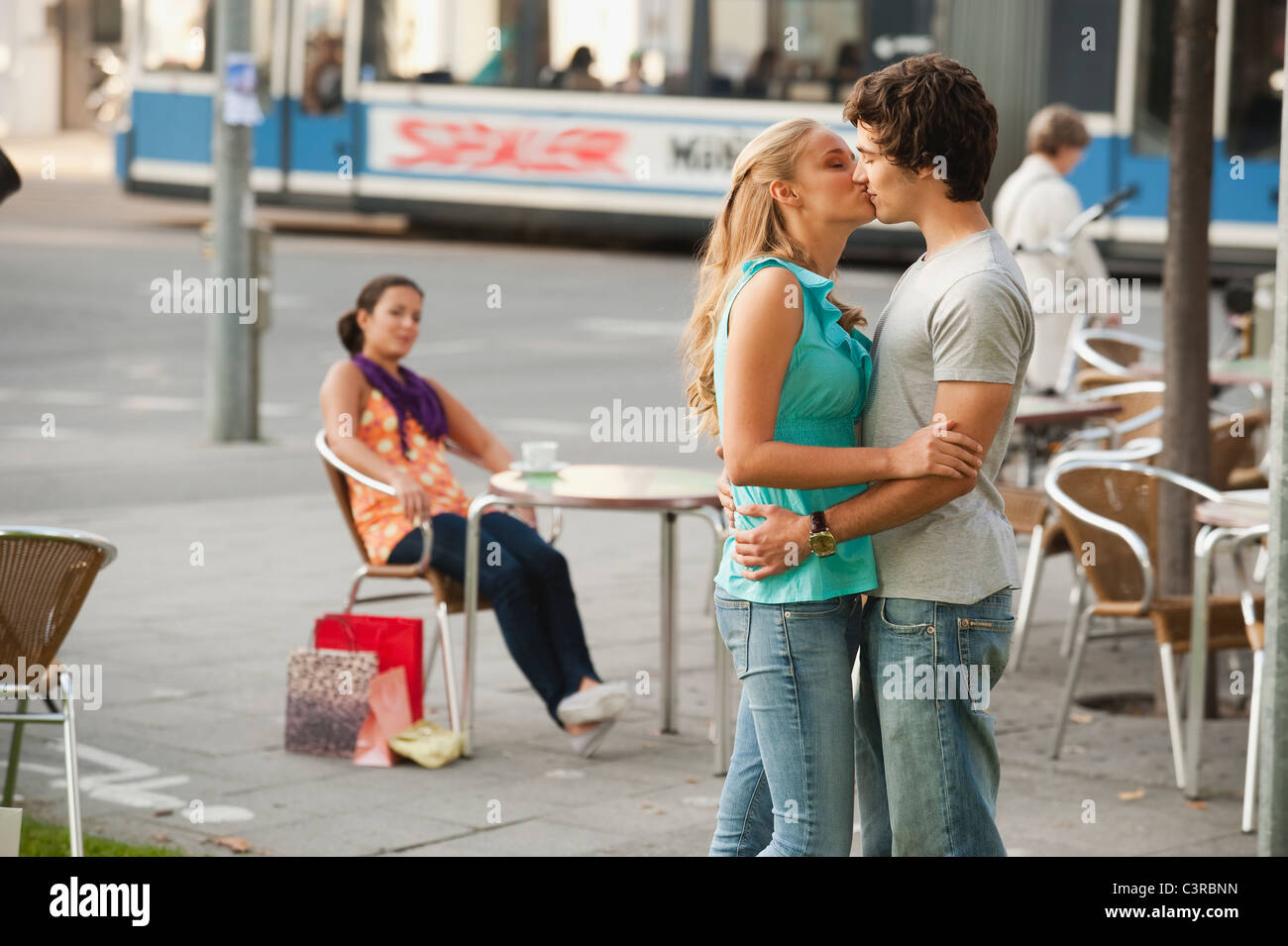 Germany, Munich, Couple kissing at cafe with woman in background Stock ...