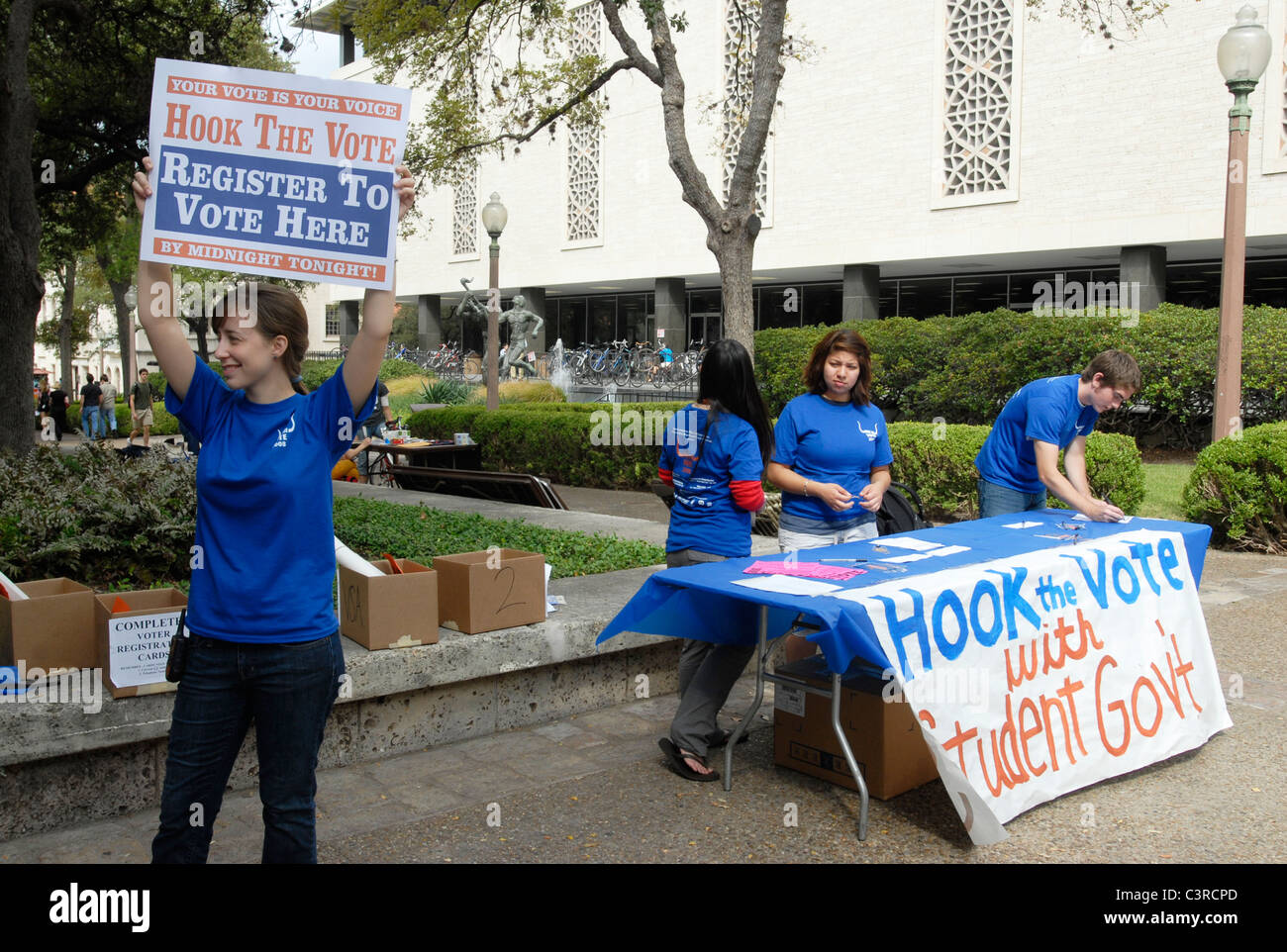 Young college students hold up sign and set up table for people to ...
