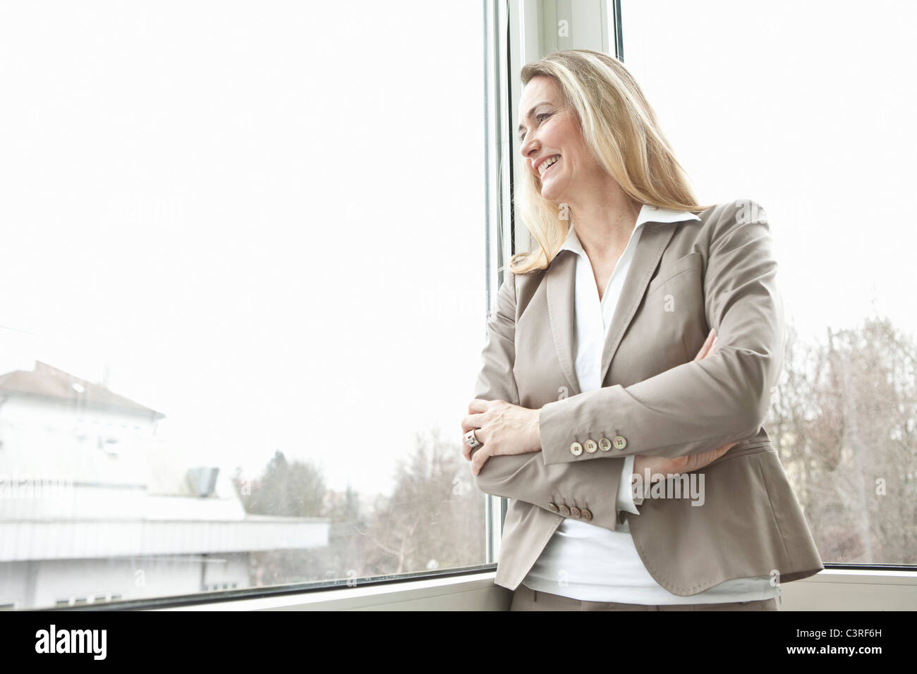 Businesswoman looking out window smiling Stock Photo - Alamy
