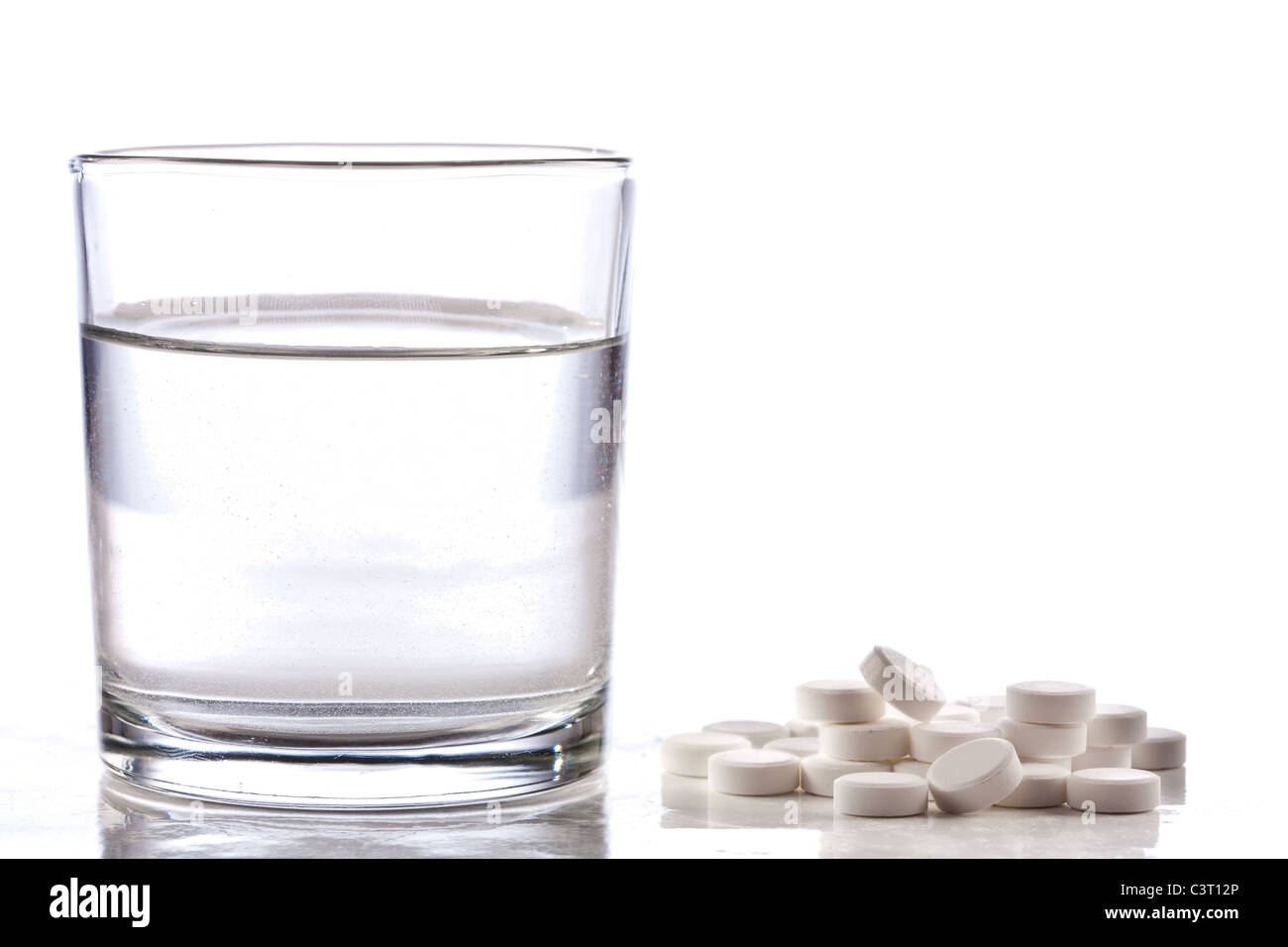 A pile of white tablets near a glass of water isolated on white ...